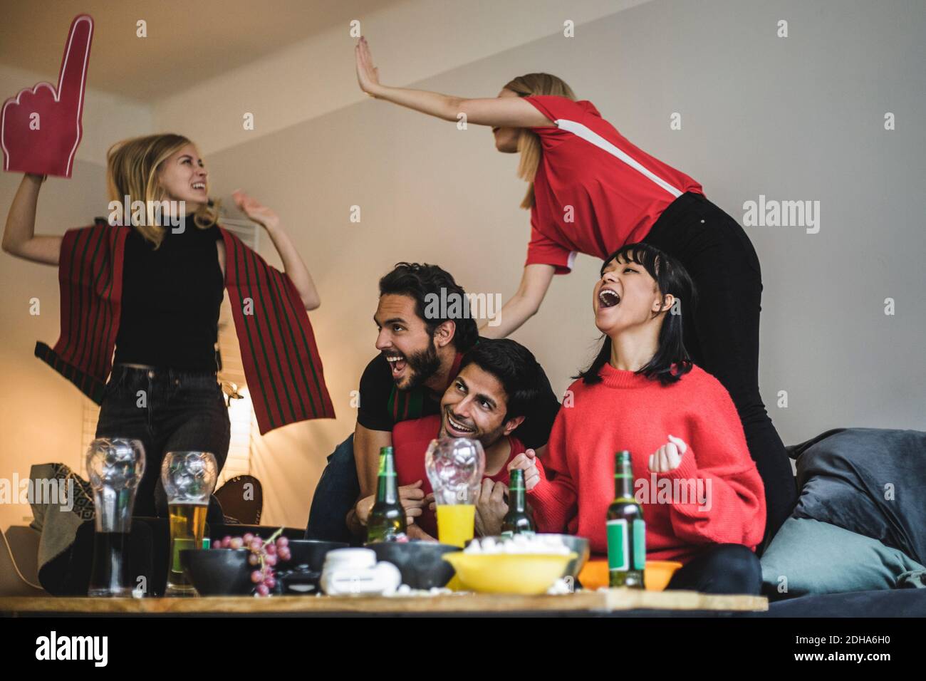 Happy male and female fans celebrating while watching soccer match at ...