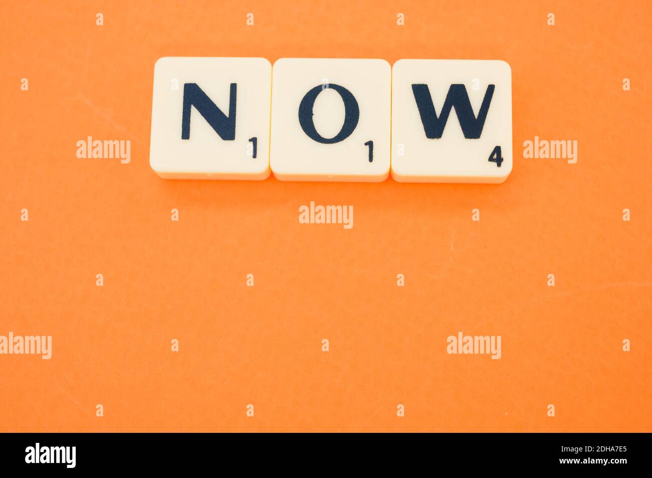 A top view of the word "Now" made of tiles on orange background for a ...