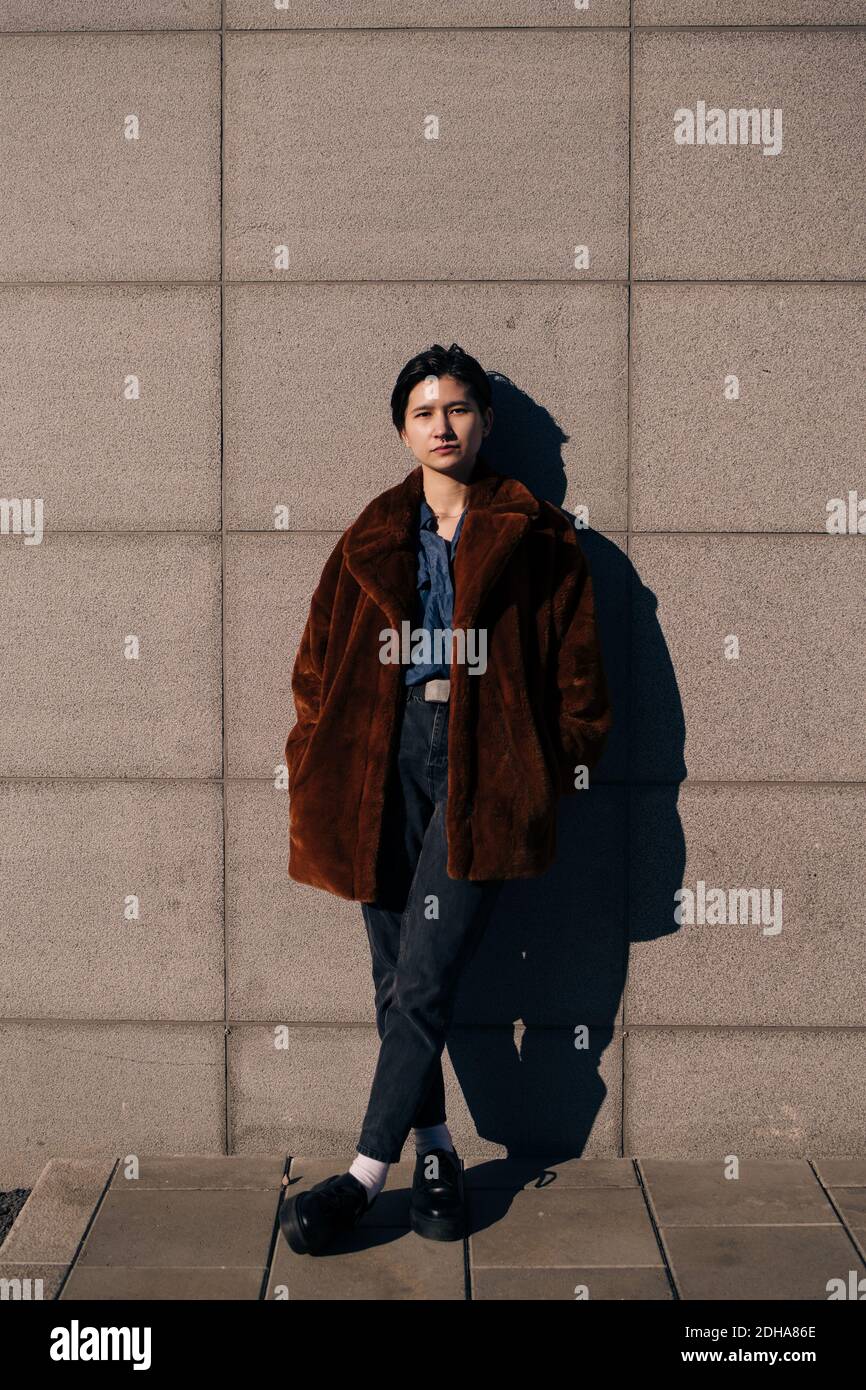 Portrait of contemplating young woman with hands in pockets standing ...