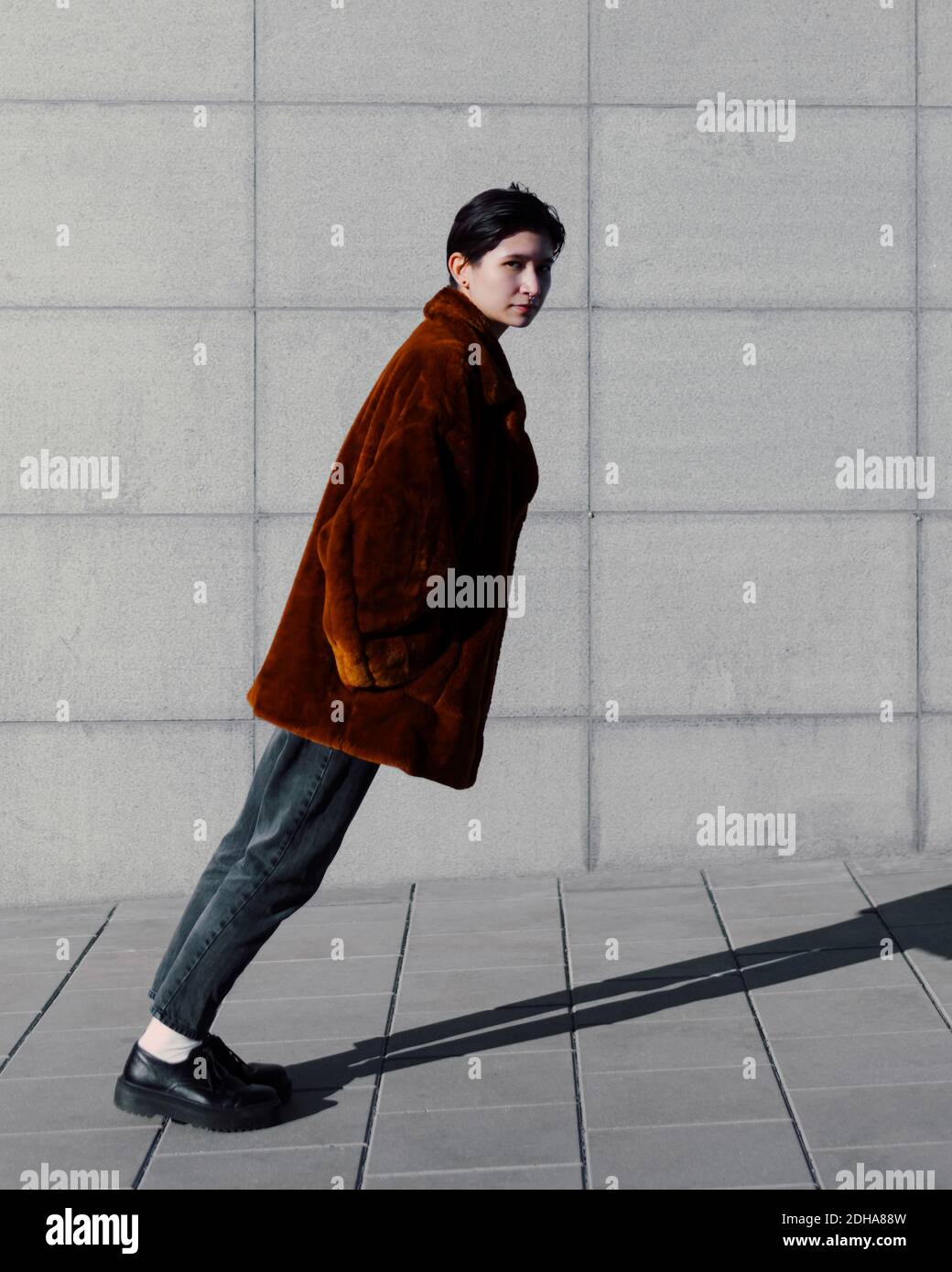 Portrait of contemplating woman with hands in pockets leaning against ...