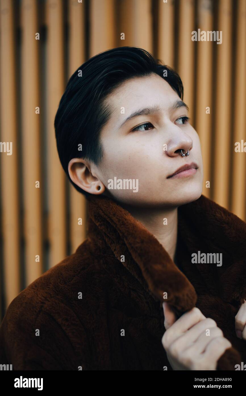 Contemplating woman in jacket standing against wooden wall Stock Photo ...