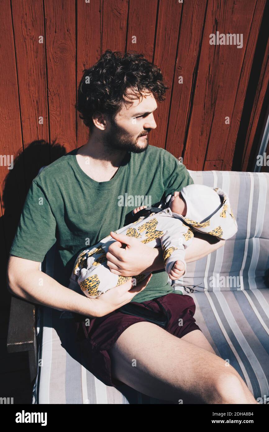 Father carrying baby boy while sitting on chair against wall during ...