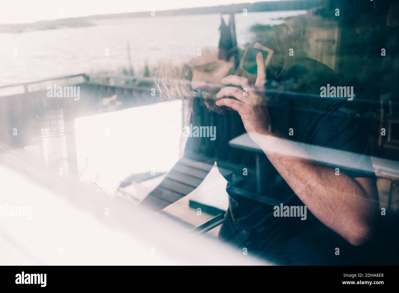 Man talking on smart phone seen through glass window with reflection of ...