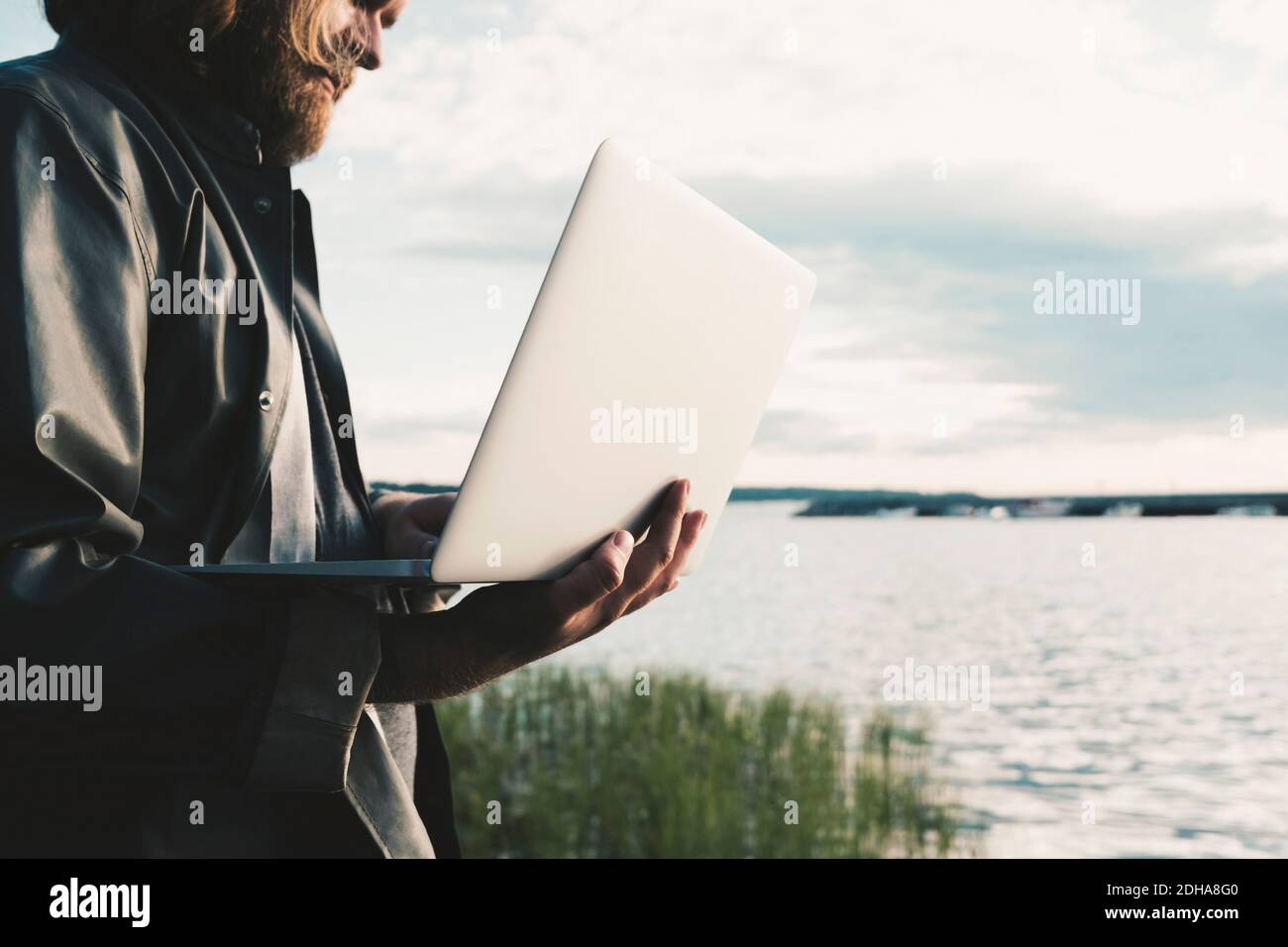 Midsection of man using laptop by lake against sky Stock Photo - Alamy