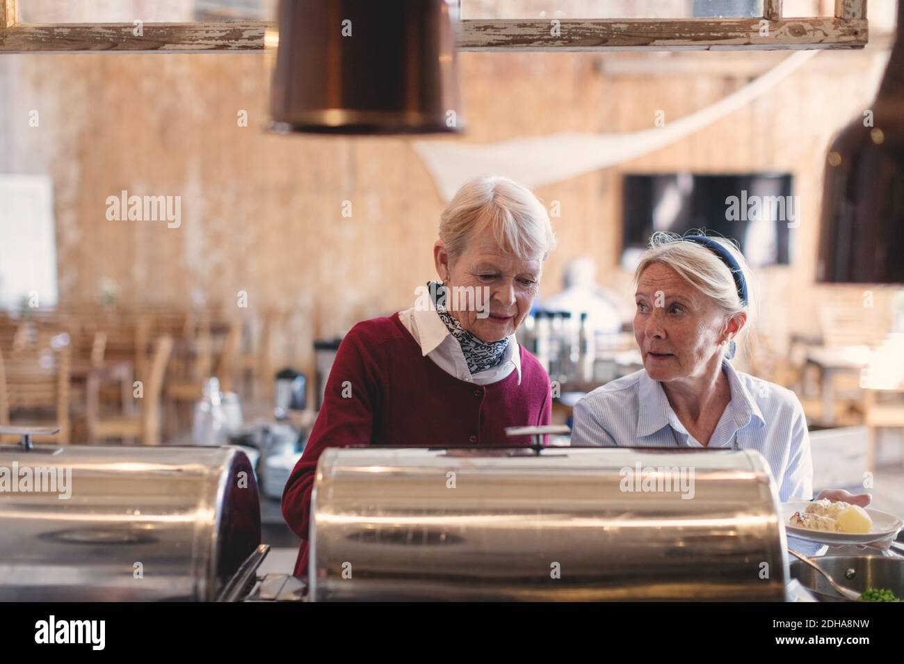Senior female friends getting food from buffet counter at restaurant ...