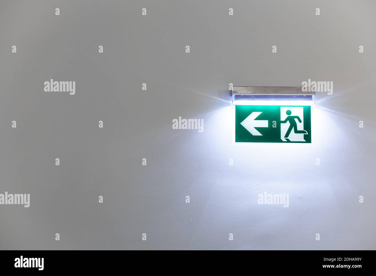green illuminated emergency exit sign on a white wall of a building ...