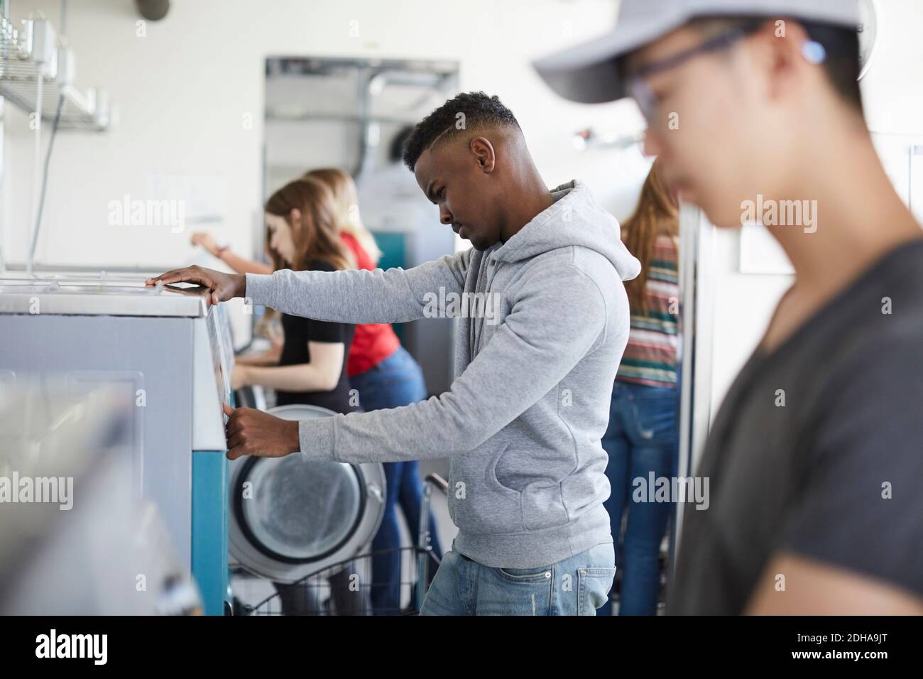 Male and female university students using washing machine at laundromat ...