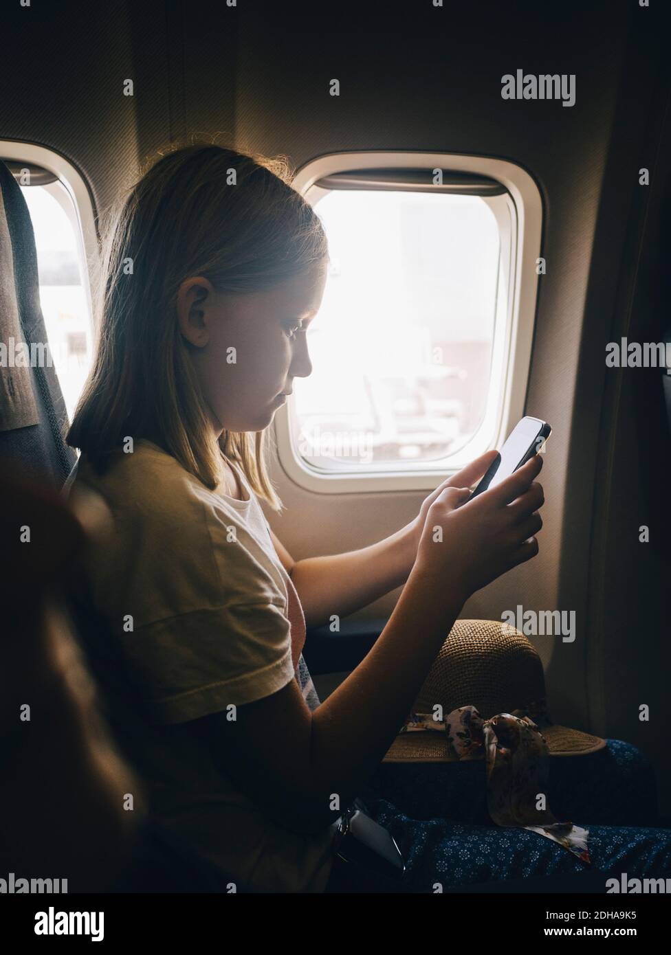 Side view of girl using mobile phone while sitting by airplane window ...
