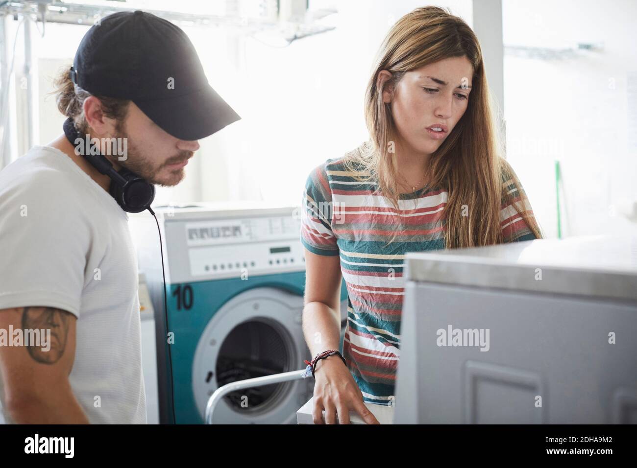 Man assisting female friend in using washing machine at laundromat ...