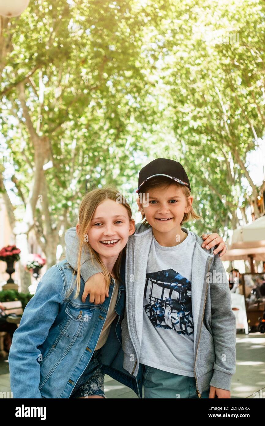 Portrait Of Smiling Brother And Sister Standing Arm Around In City
