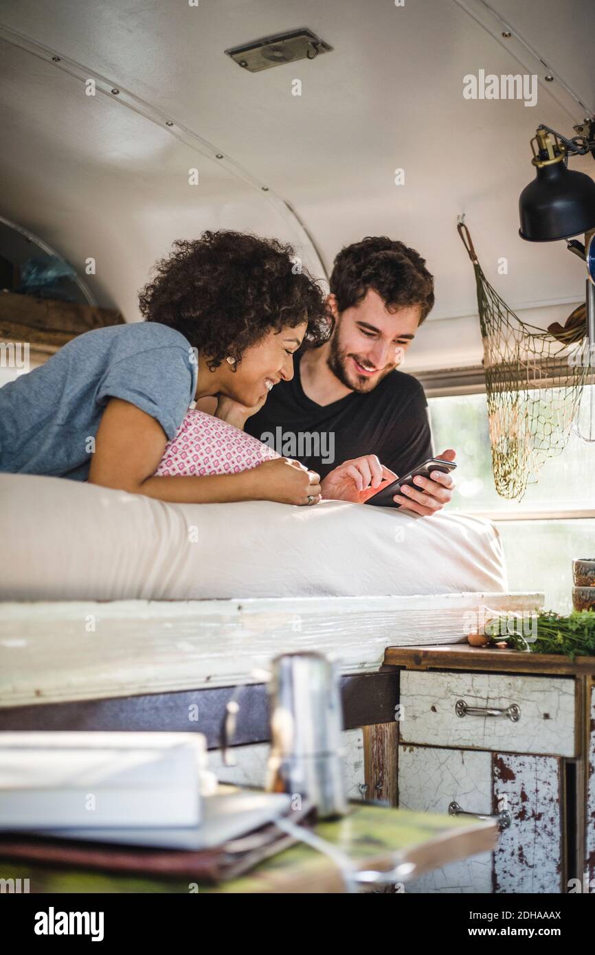 Smiling couple sharing mobile phone while lying on bed in caravan Stock ...