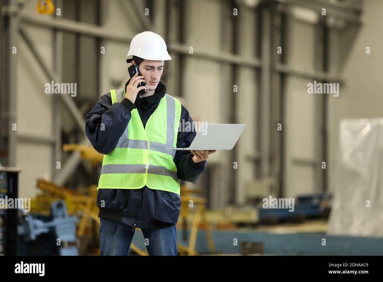 Young man, factory engineer in a work dress and white hard hat holding ...