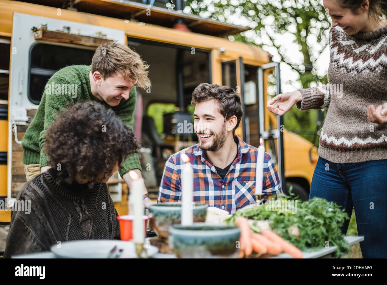 Cheerful friends enjoying camping at table against caravan Stock Photo ...