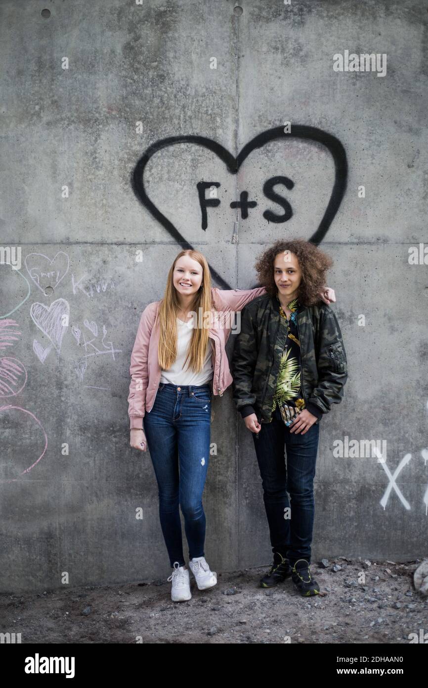 Full length portrait of smiling friends standing against graffiti on ...