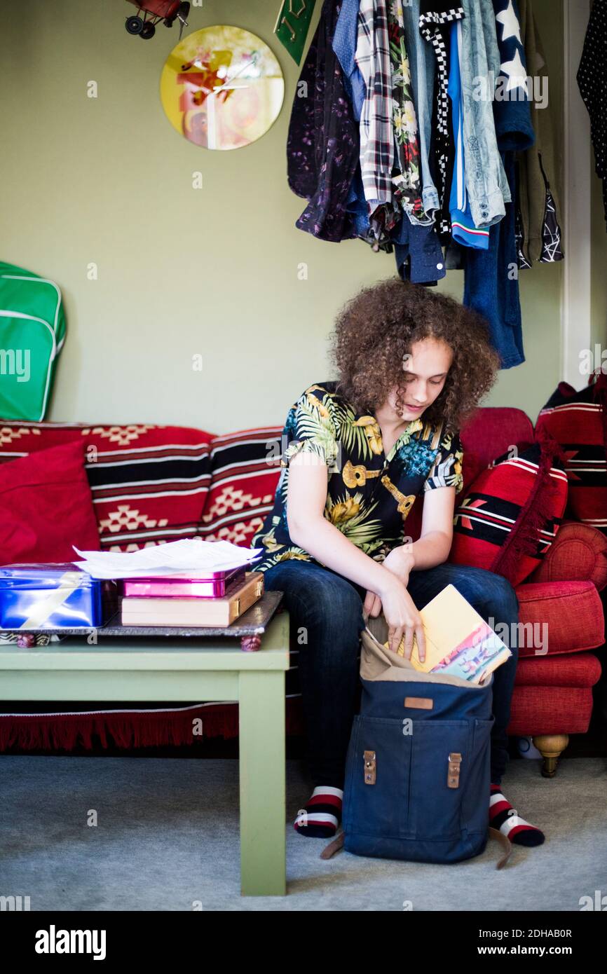 Full length of teenage boy putting books in backpack while sitting on ...