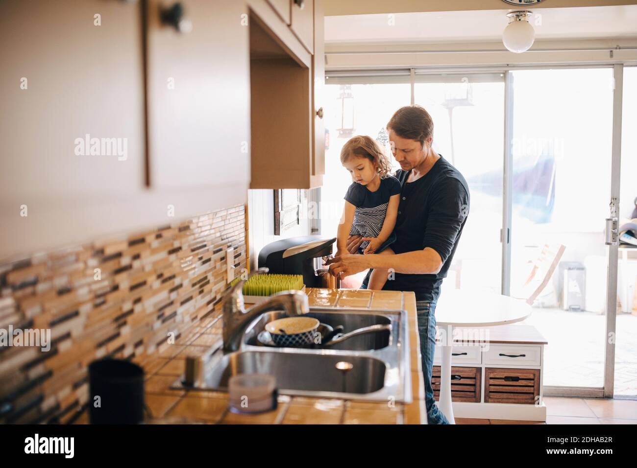 Father making coffee while carrying daughter at home Stock Photo - Alamy
