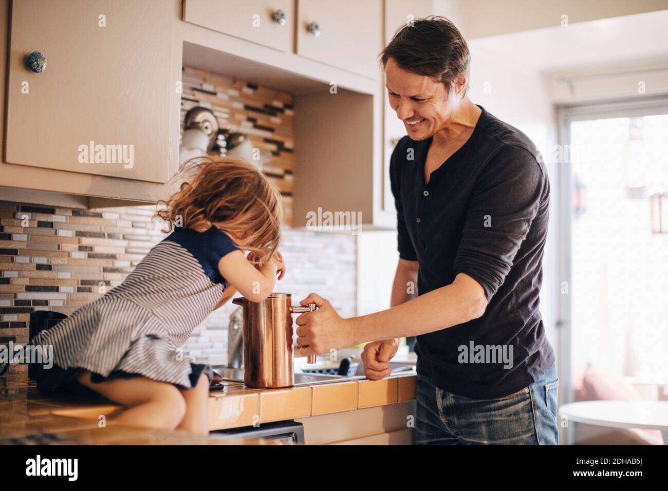 Happy father looking at daughter pushing french press while sitting on ...