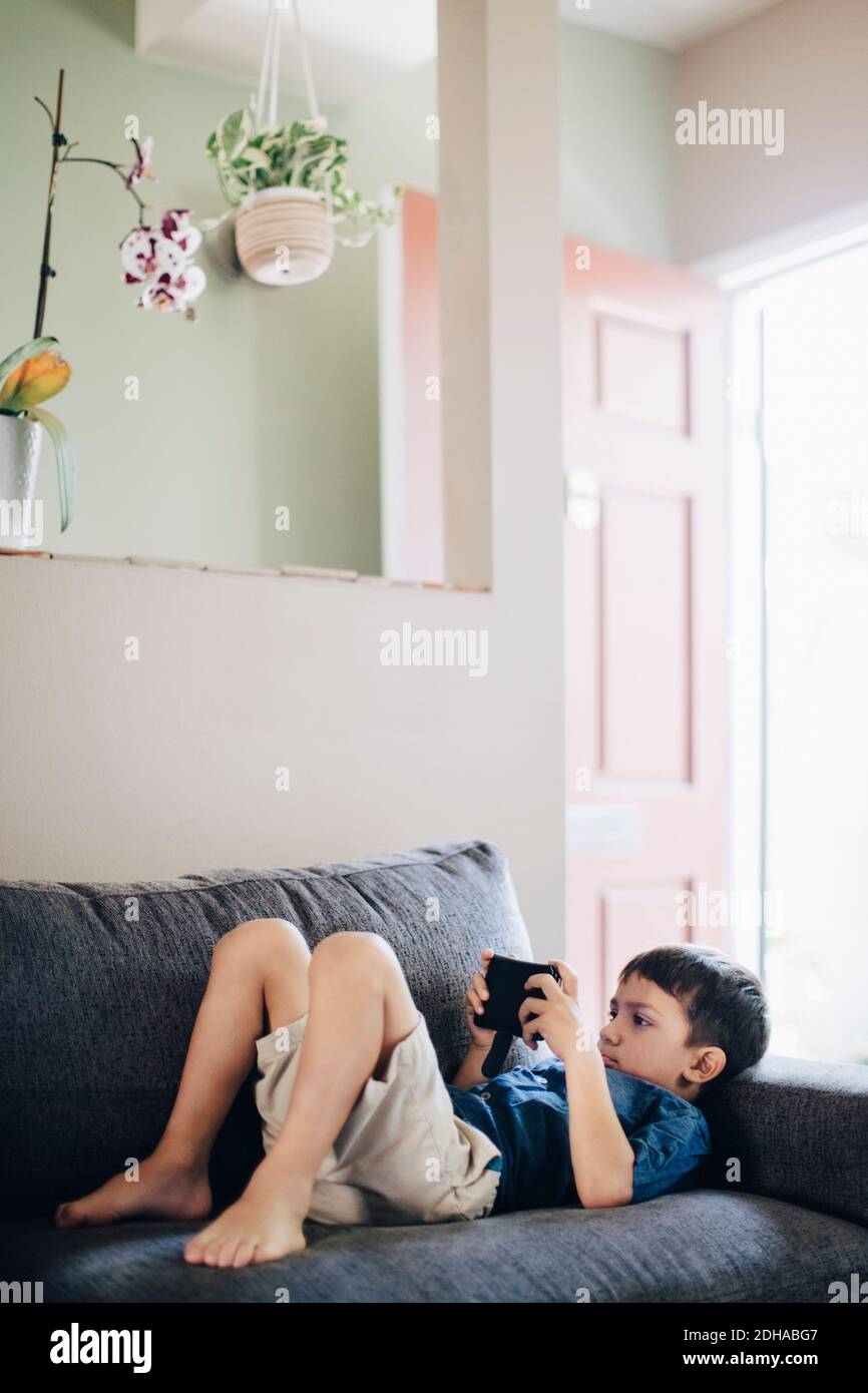 Boy using phone while lying on sofa at home Stock Photo - Alamy