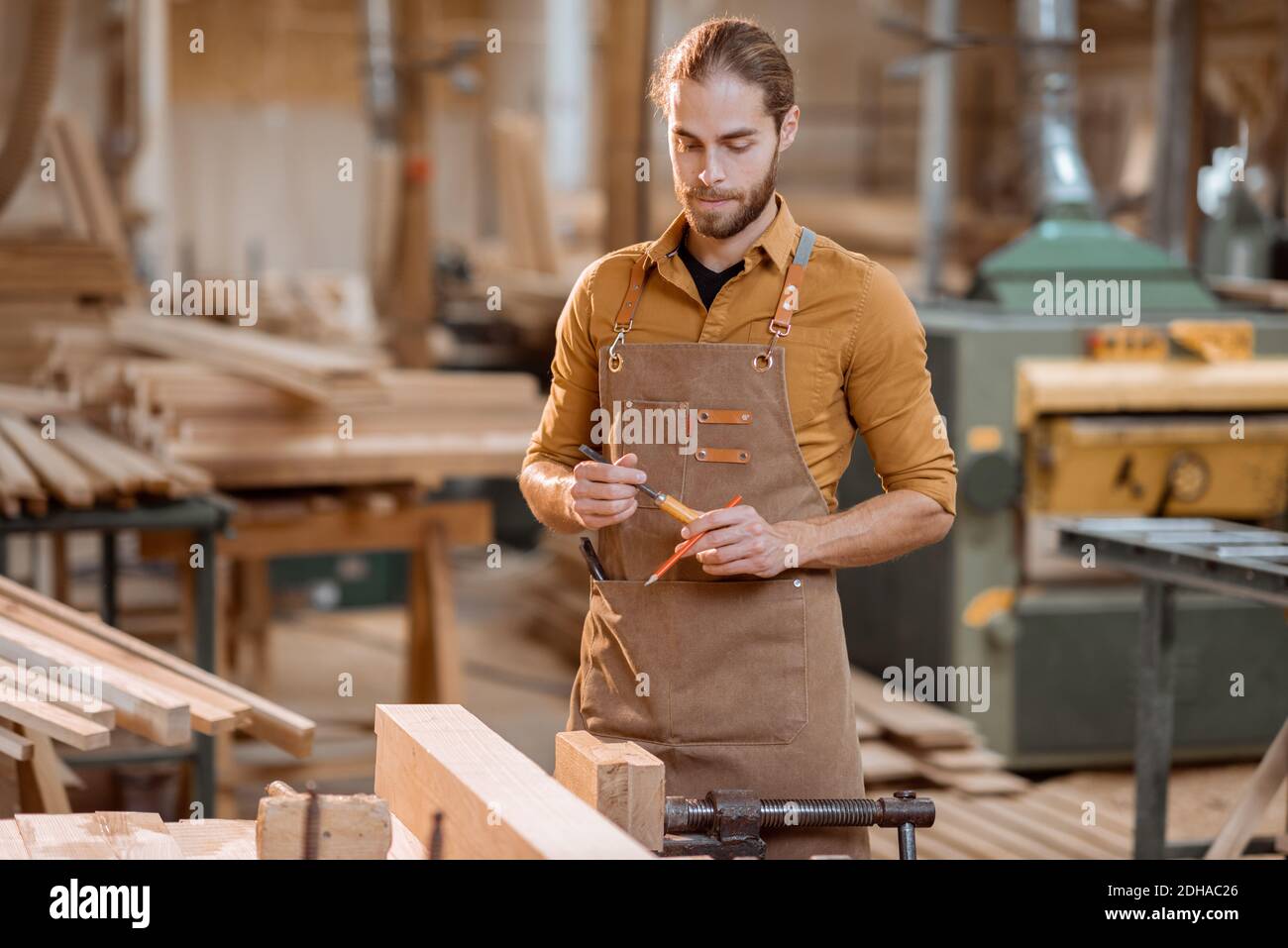 Portrait of a handsome carpenter, standing near the workbench at the ...
