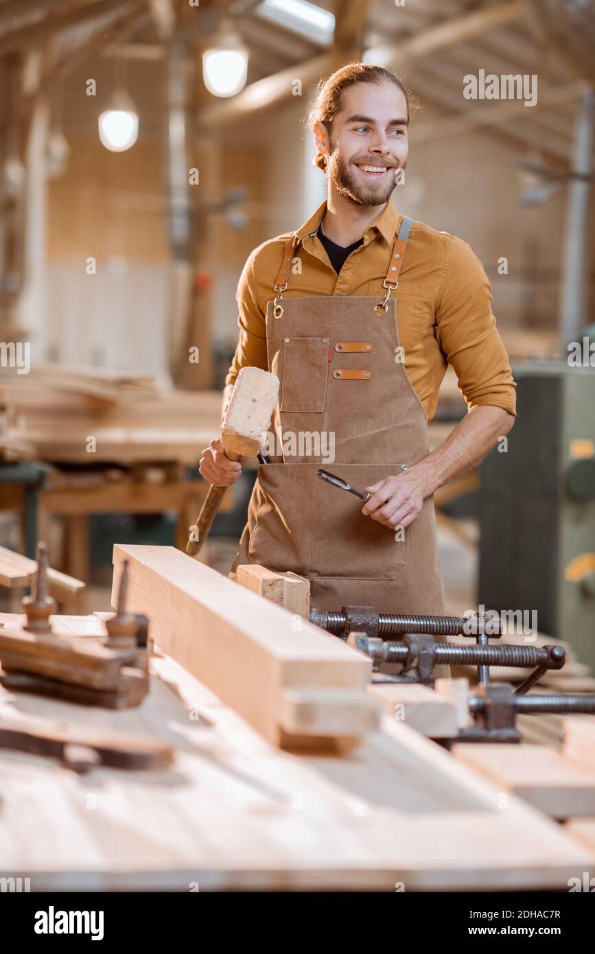 Portrait of a handsome carpenter, standing near the workbench at the ...