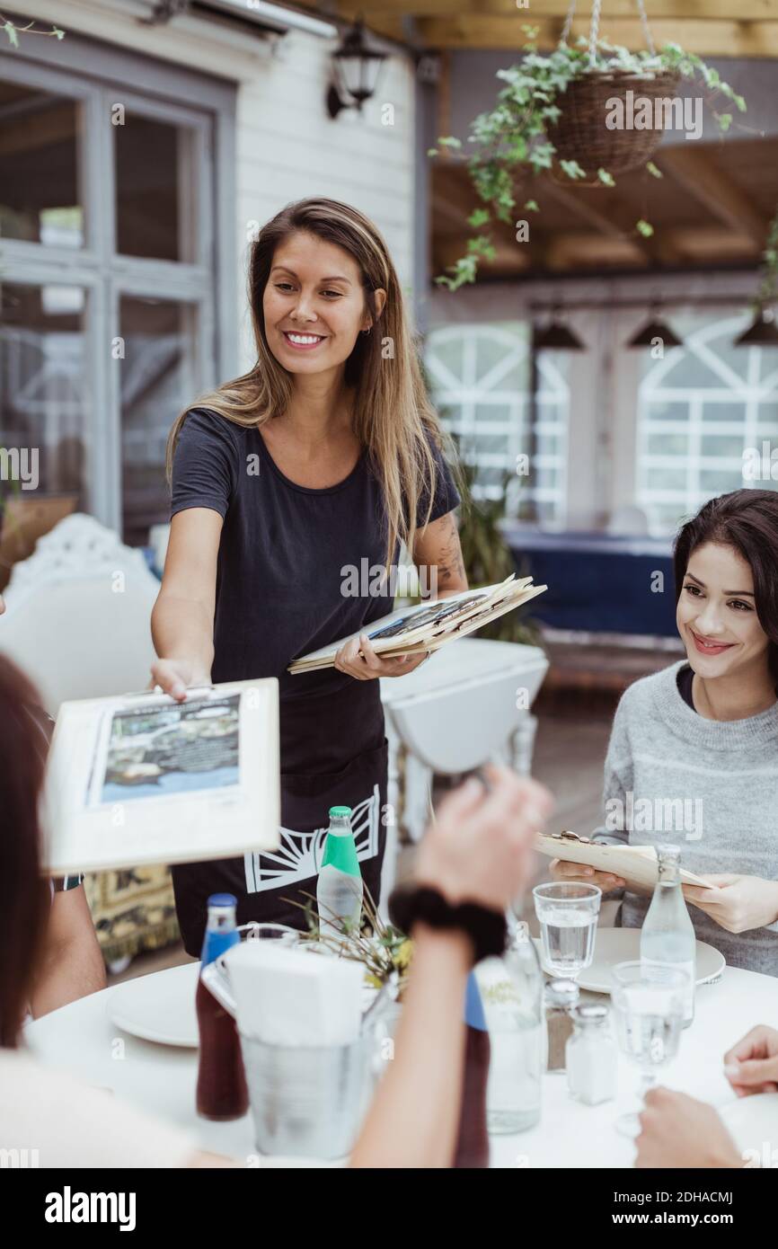 Smiling female owner giving menu cards to customer sitting in ...