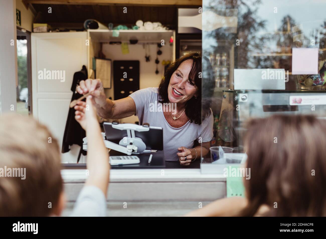 Smiling female owner giving spoon to customer standing by concession ...
