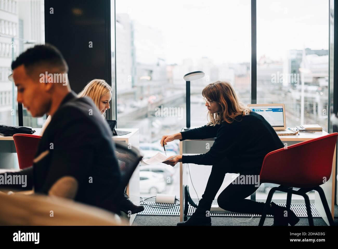 Side view of businessman working against female colleagues discussing ...