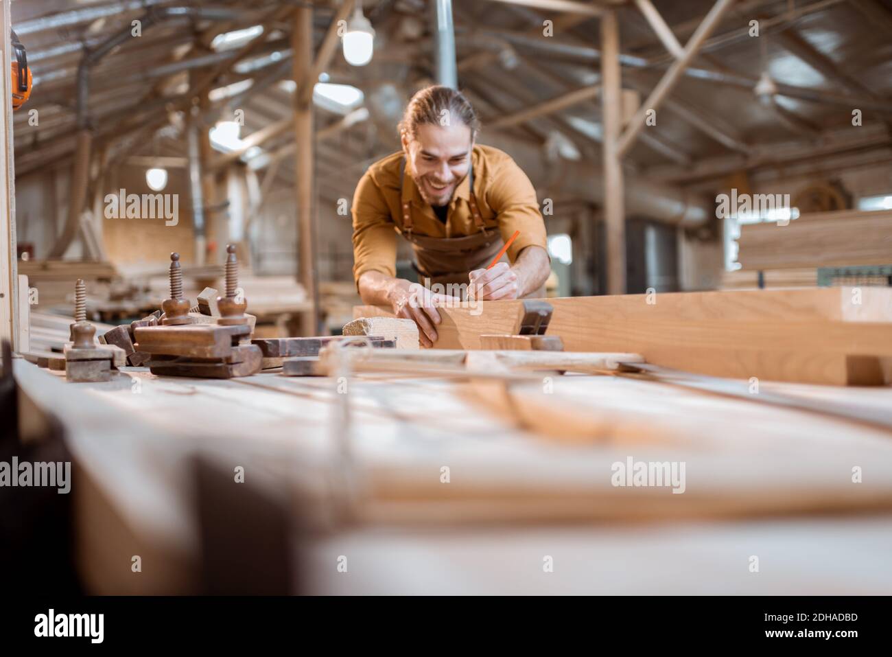 Handsome carpenter working with a wood, planing a bar with a plane in ...