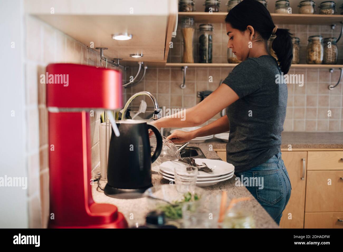 Side view of woman washing utensils in kitchen sink at home Stock Photo ...