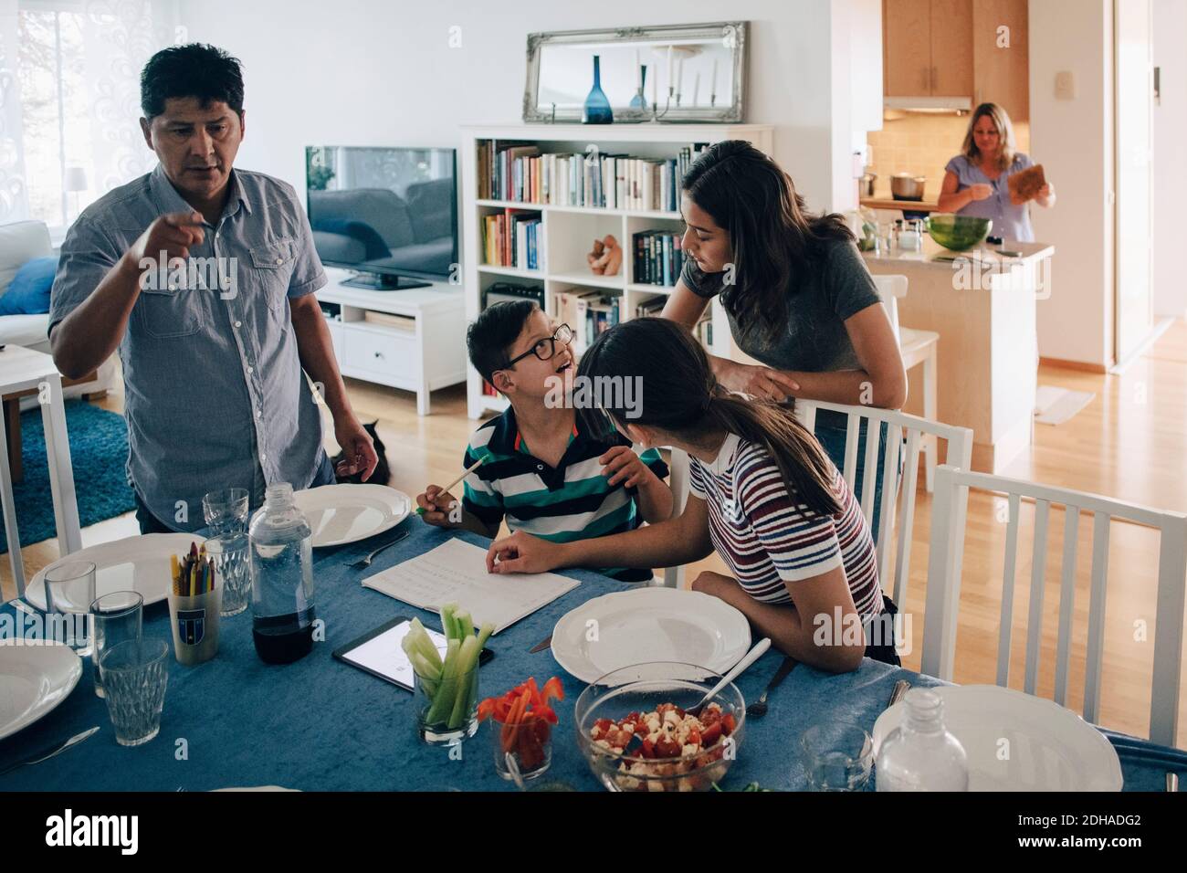 Sisters looking at boy while father standing by dining table Stock ...