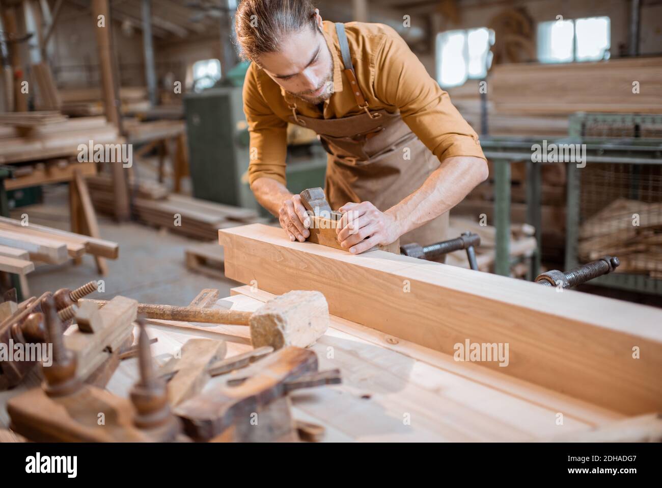 Handsome carpenter working with a wood, planing a bar with a plane in ...