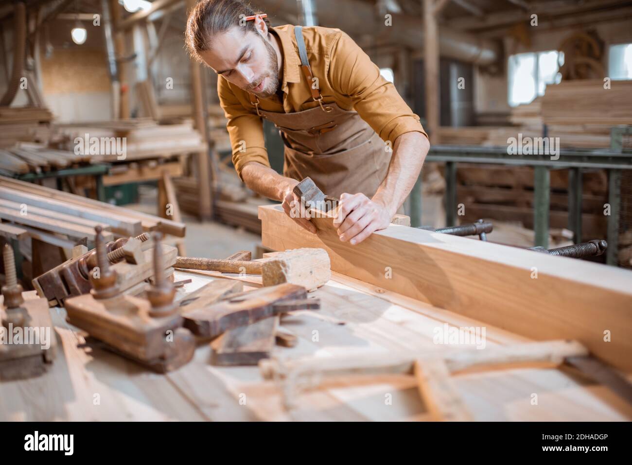 Handsome carpenter working with a wood, planing a bar with a plane in ...