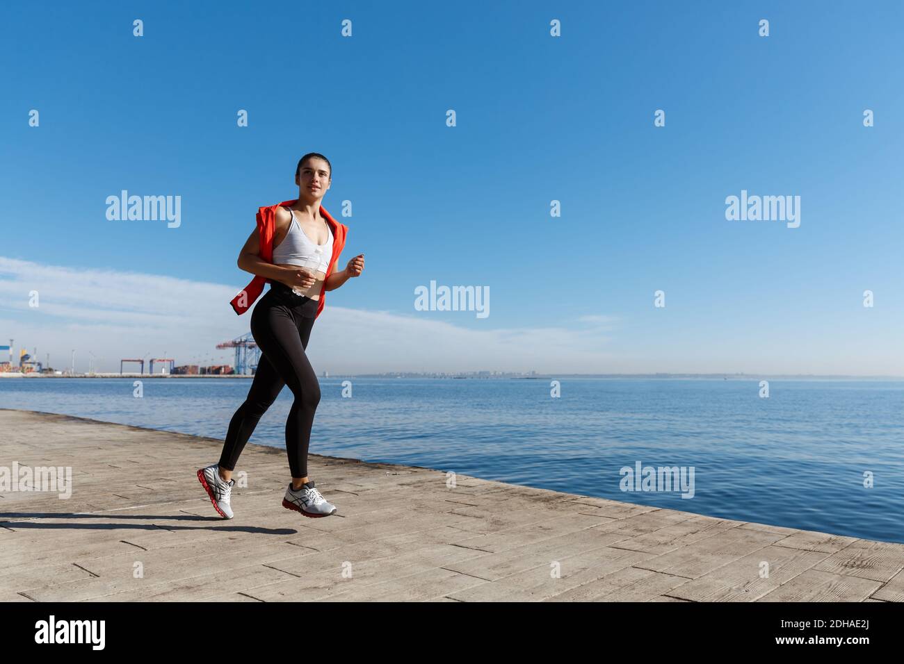 Side view of athletic young woman running along the seaside promenade ...