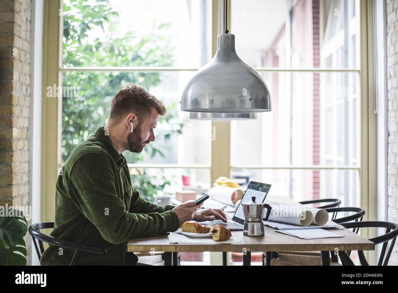 Male entrepreneur using laptop while holding phone at home office Stock ...