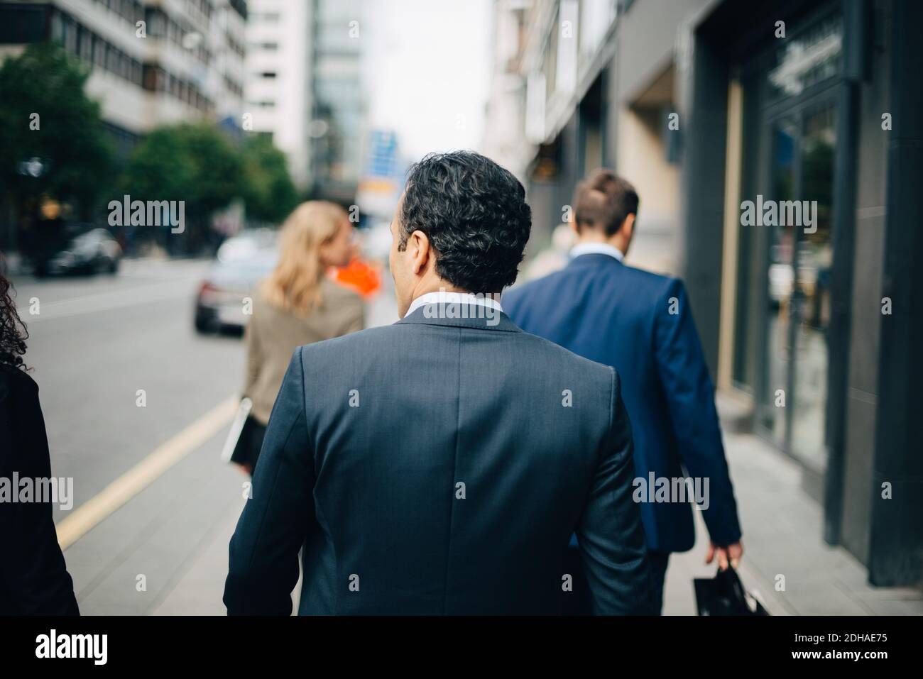 Rear view of businessman walking behind colleagues on sidewalk in city ...