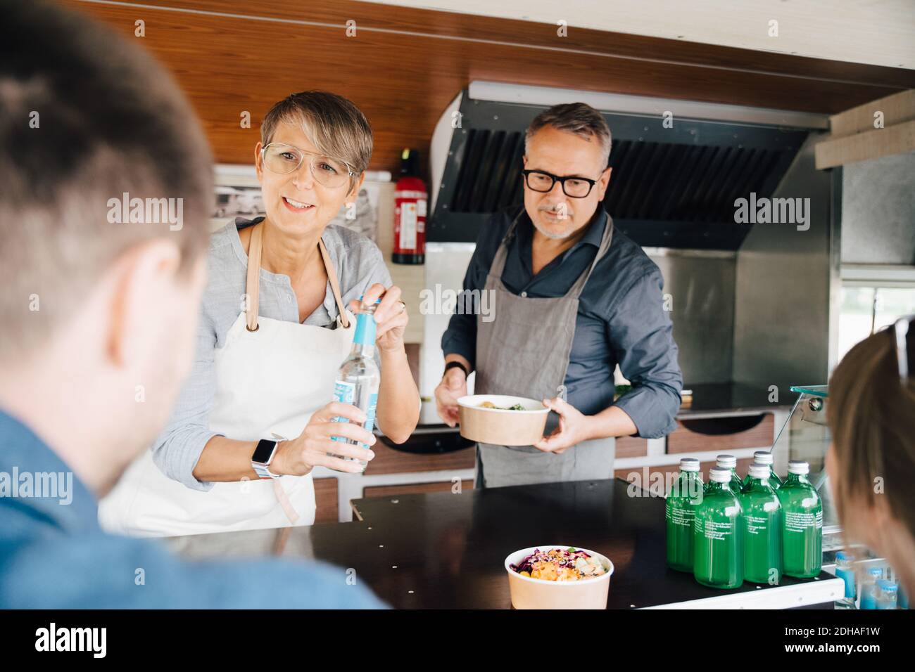 Mature owners serving food and drink to customers while standing in ...