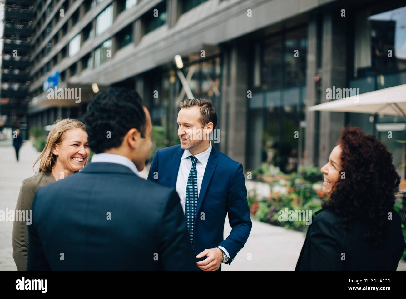 Cheerful business colleagues talking while standing against building in ...