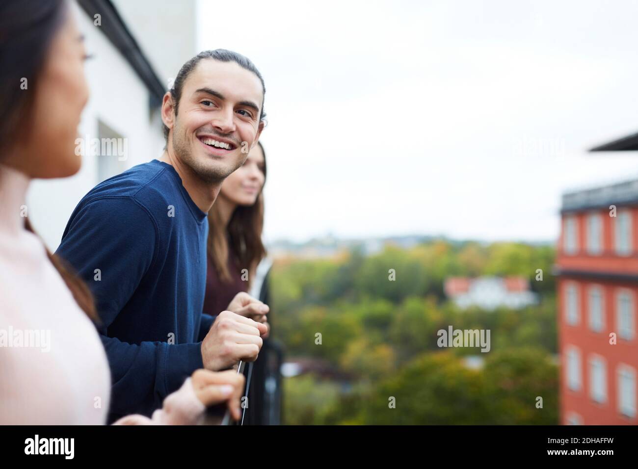 Smiling young man with female friends standing in balcony at city Stock ...