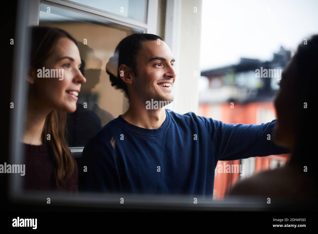 Smiling man with friends looking through window while standing in ...