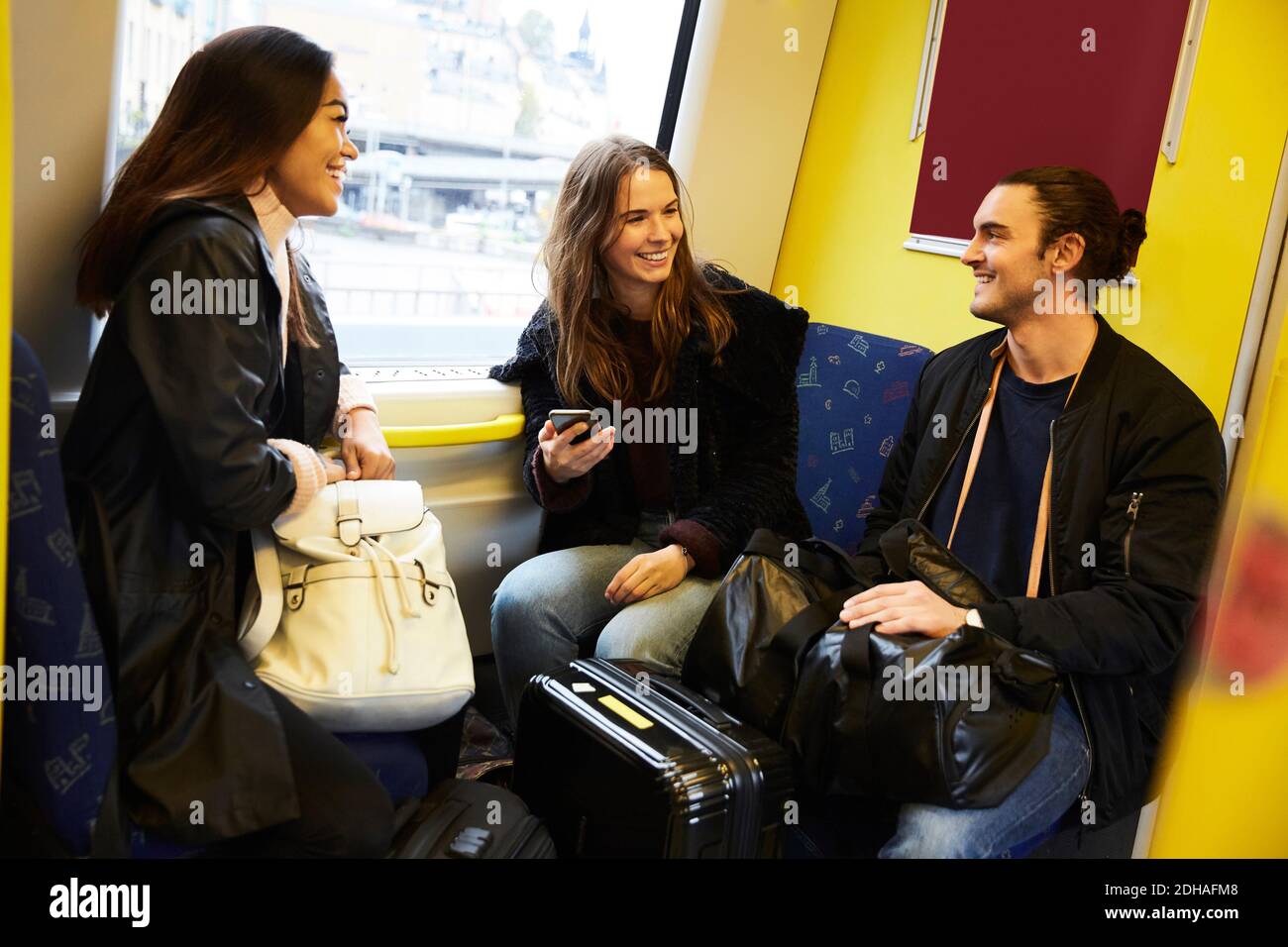 Happy young friends talking while traveling in yellow train Stock Photo ...