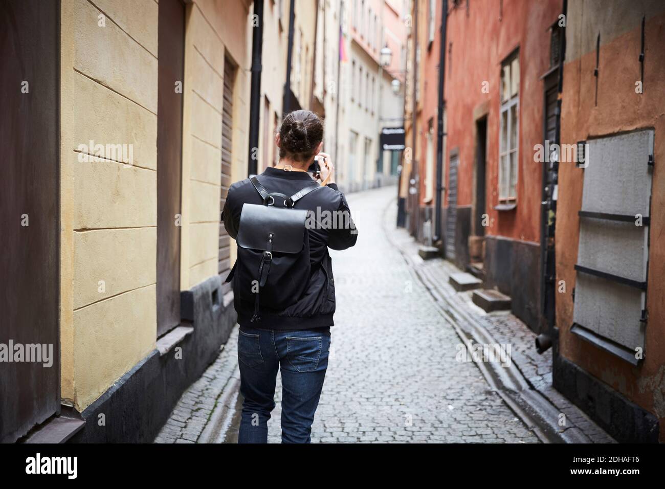 Rear view of man photographing through camera while standing on cobbled ...