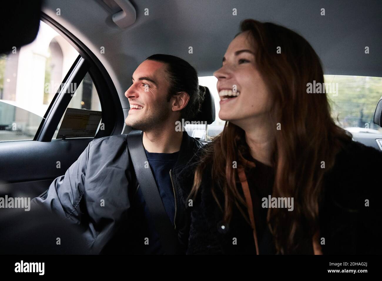 Smiling male and female friends looking through window while riding in ...