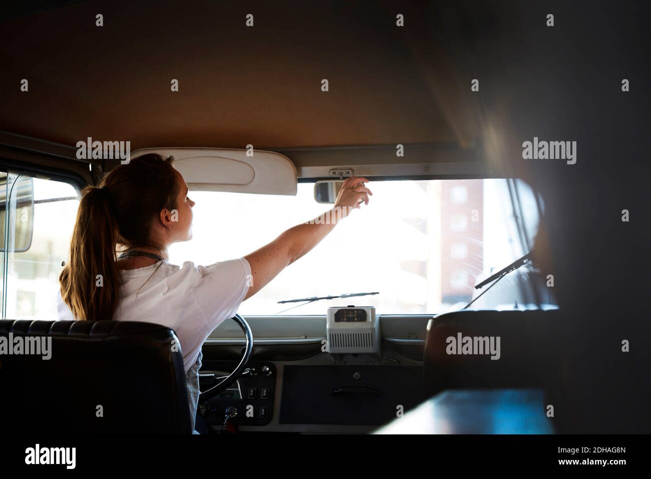 Rear view of female owner adjusting rear-view mirror in food truck ...
