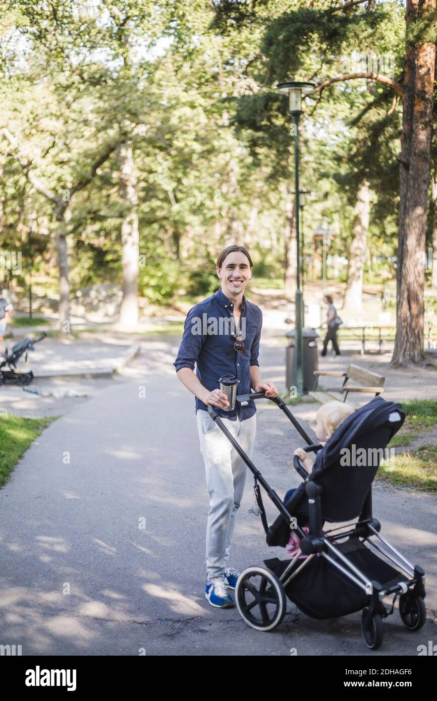 Full length portrait of smiling man standing with son on baby stroller ...