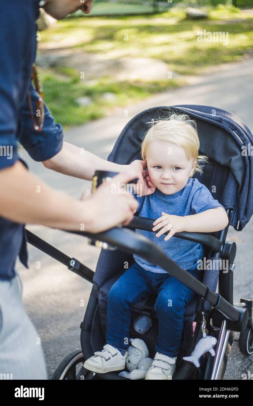 Midsection of man touching son sitting on baby carriage at public park ...