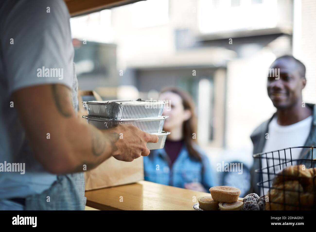 Male owner holding takeaway packaged food for customers at concession ...