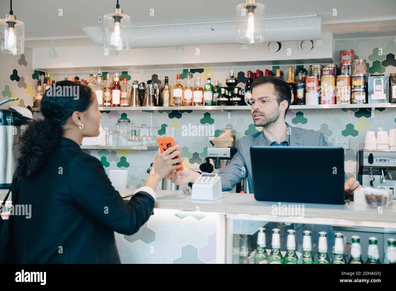 Businesswoman showing smart phone to owner at checkout counter in ...