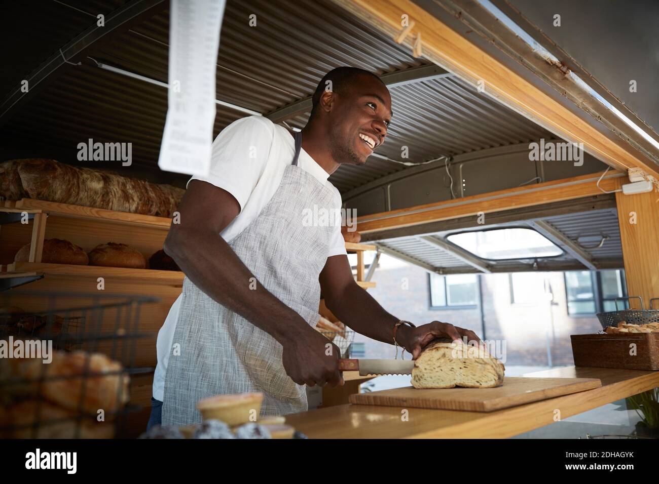 Smiling salesman slicing bread while standing in food truck Stock Photo ...