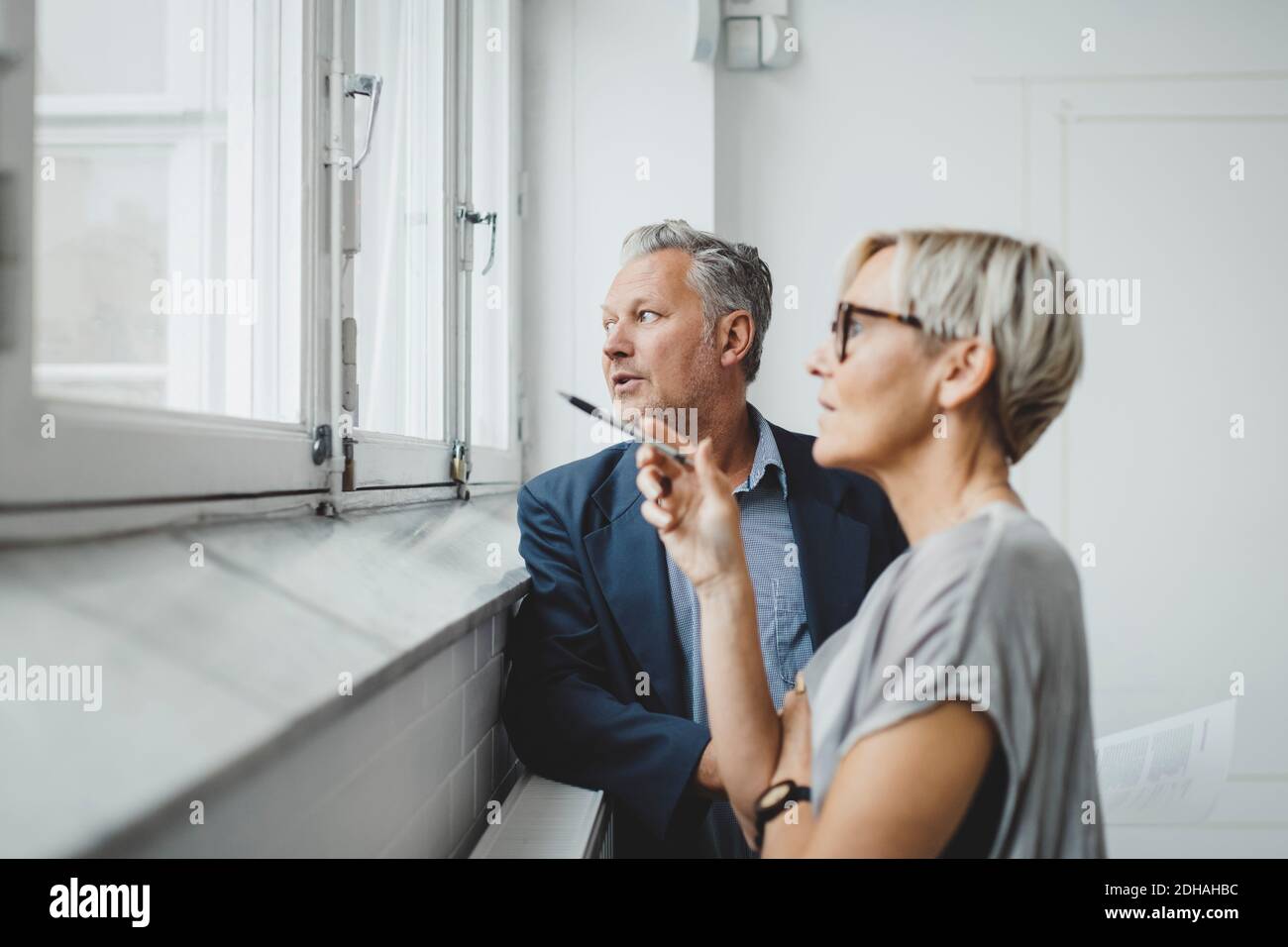 Business people looking through window while discussing in new office ...
