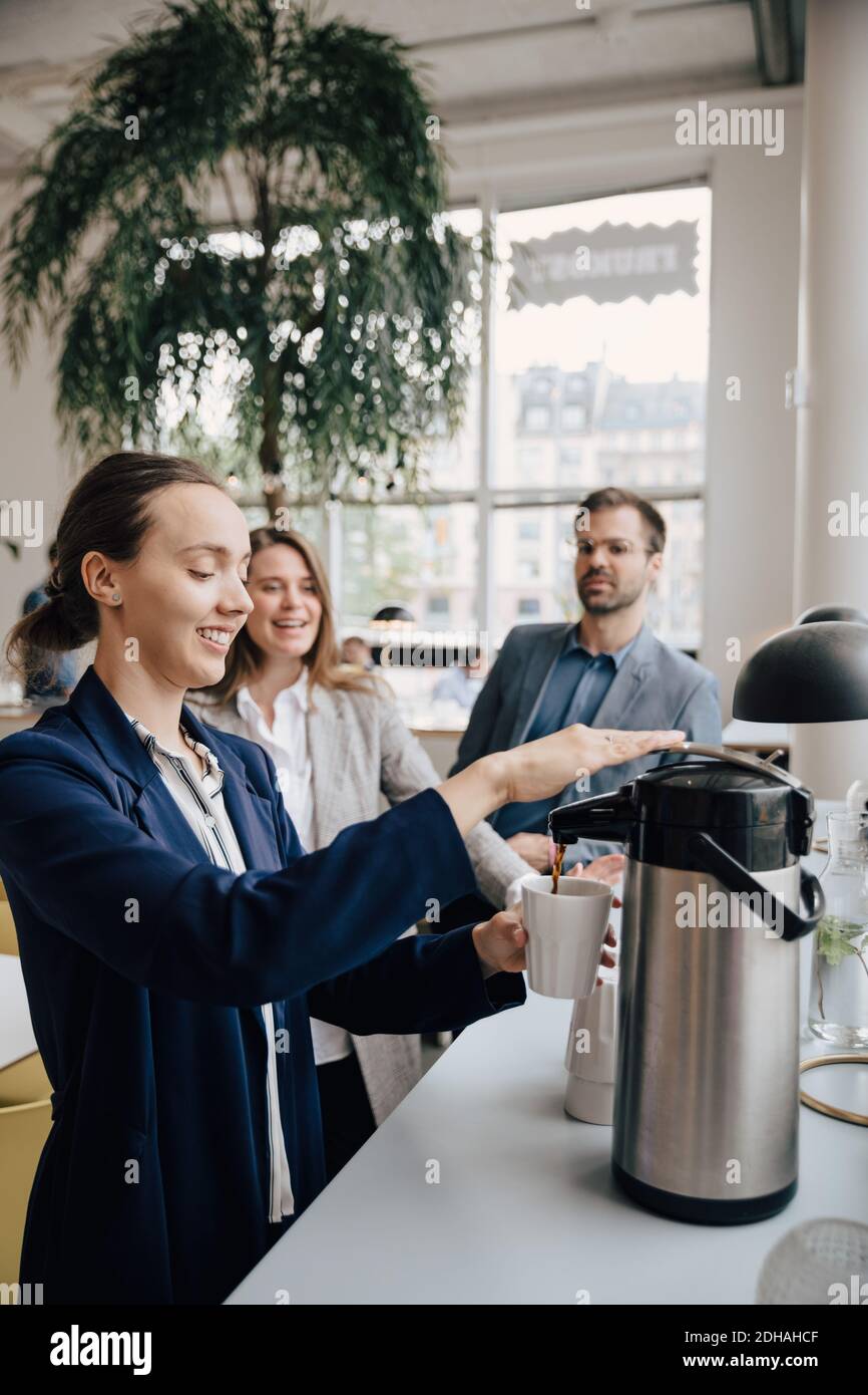 Smiling colleagues looking at businesswoman having coffee during break ...